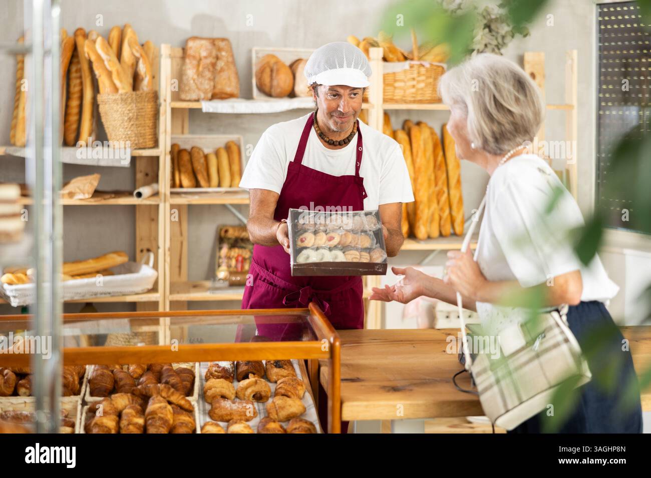 Male owner of bread shop shows for senior woman customer cookies in box ...