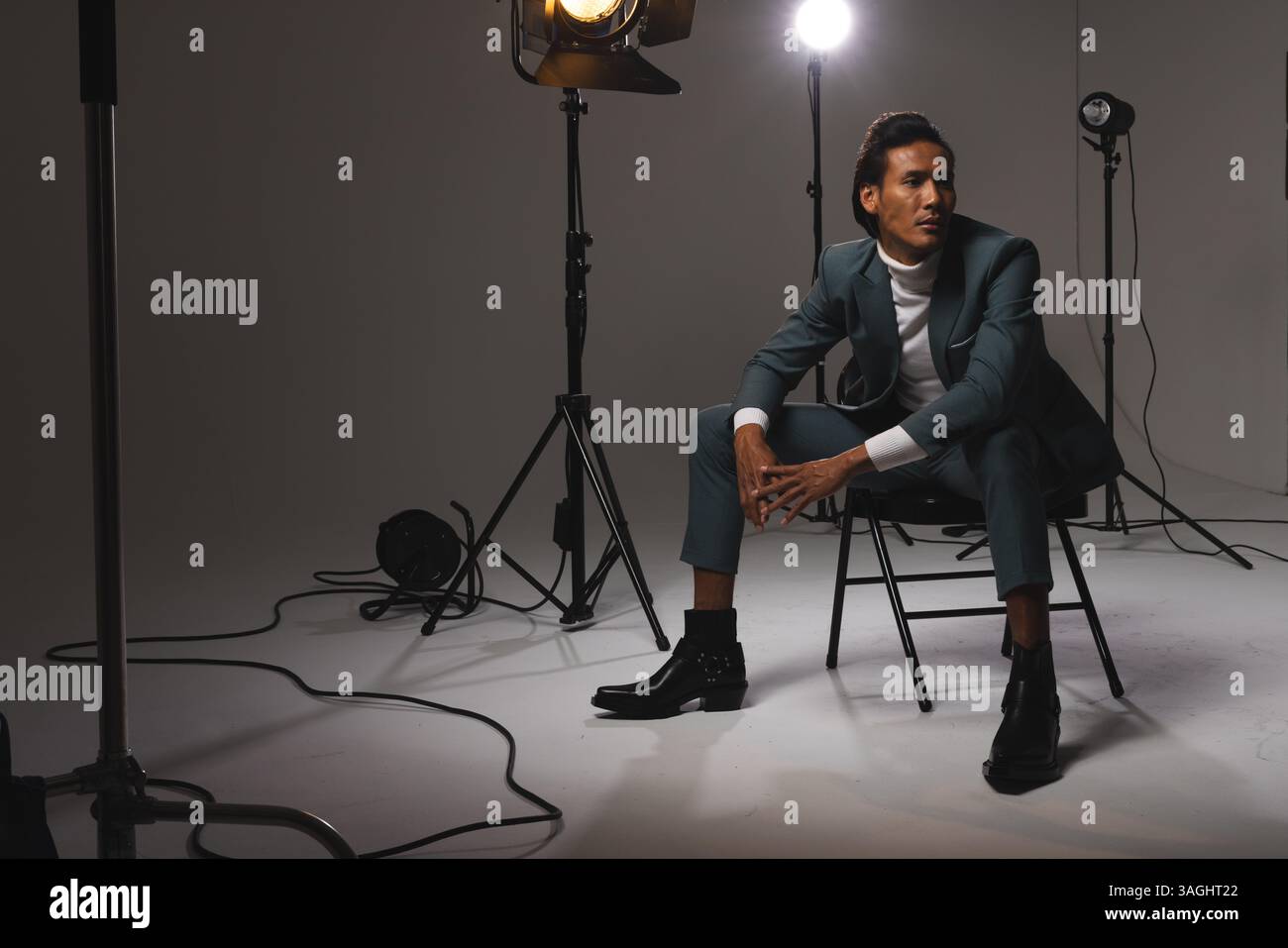 Fashion model in stylish suit sitting on chair under studio lights ...