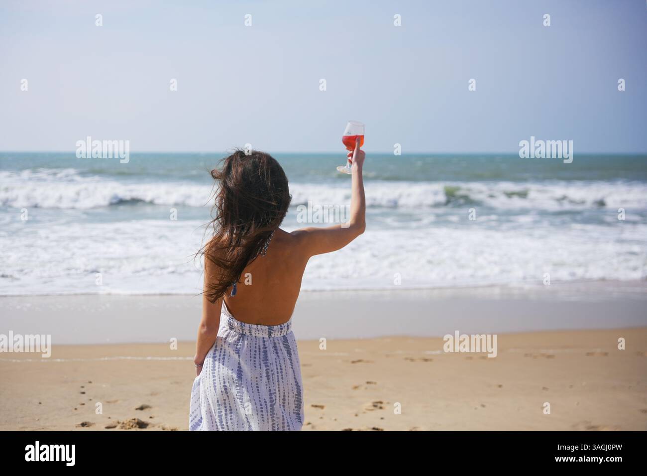 Refreshing beach moment with woman raising cocktail in flowing summer ...