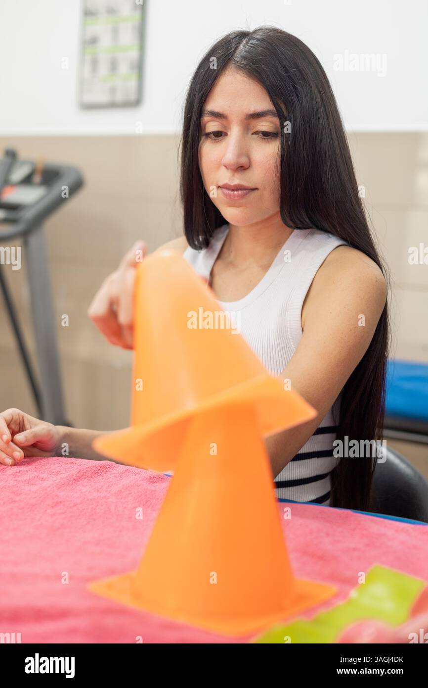 During a therapy session, a woman stacks orange cones to improve hand ...
