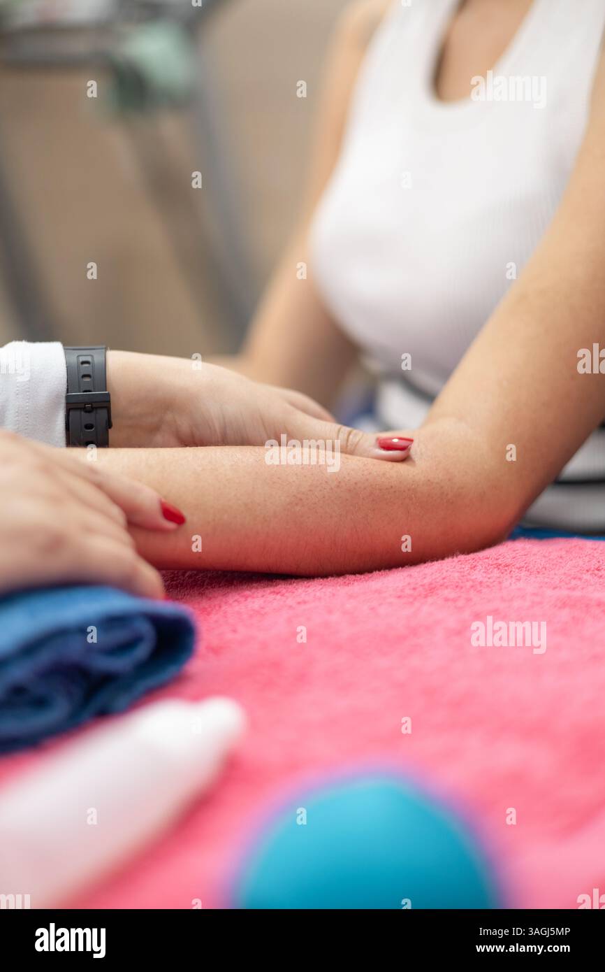 Therapist gently massages a woman’s forearm on a pink towel in a ...