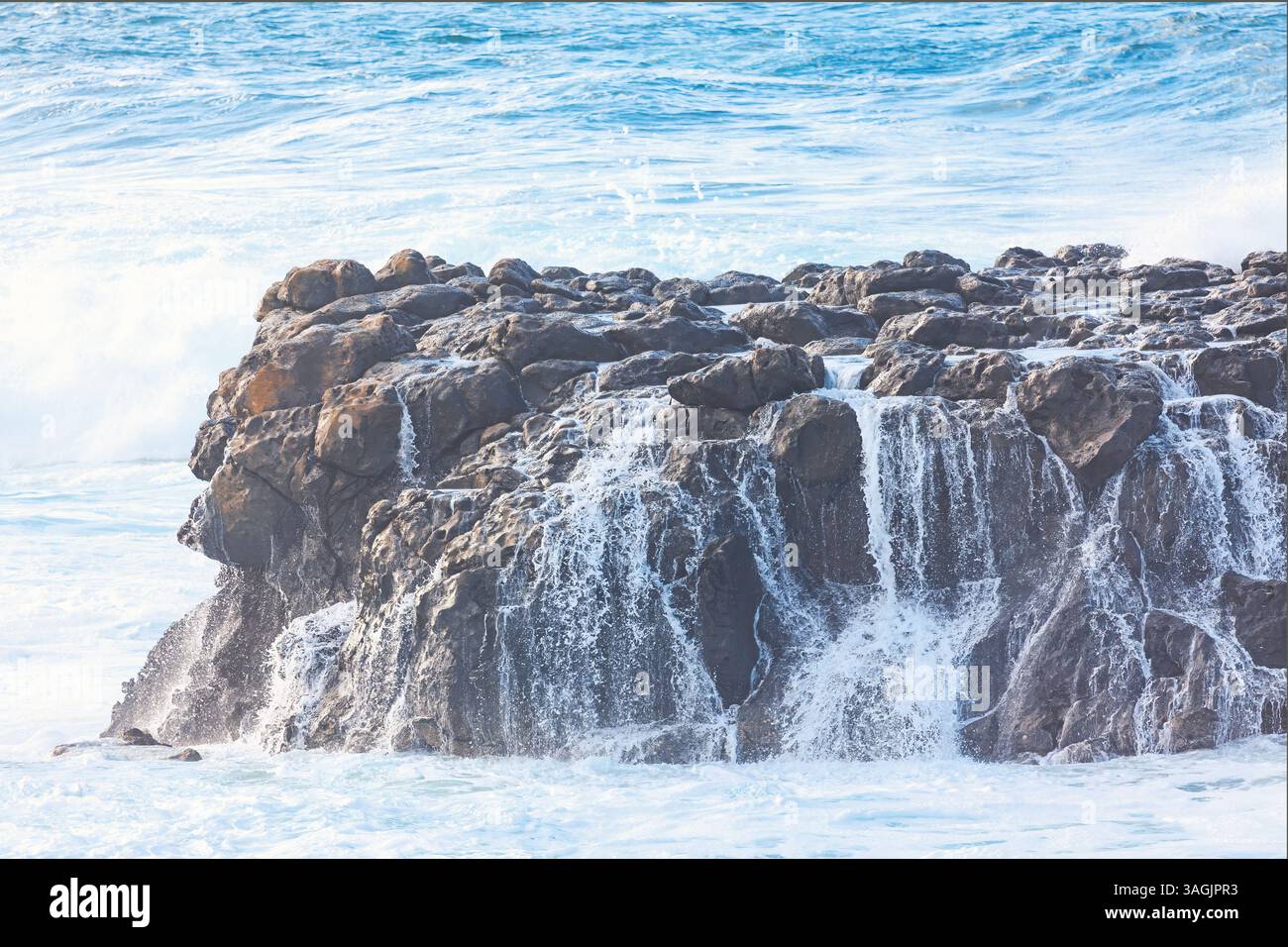 Ocean waves crash against a rugged volcanic rock formation, creating ...