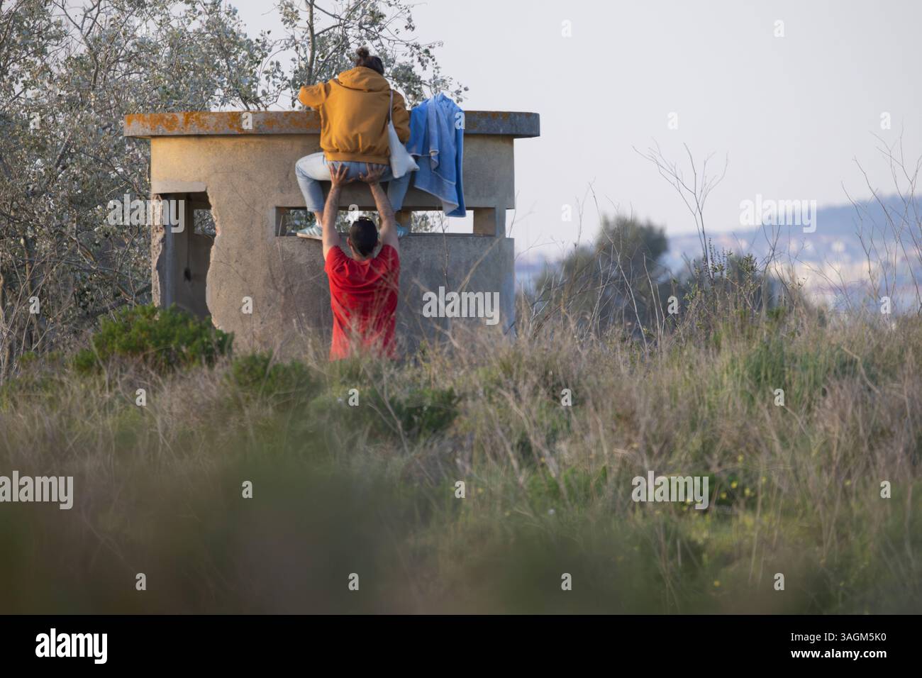 Man lifting woman onto abandoned bunker in tall grass field Stock Photo ...