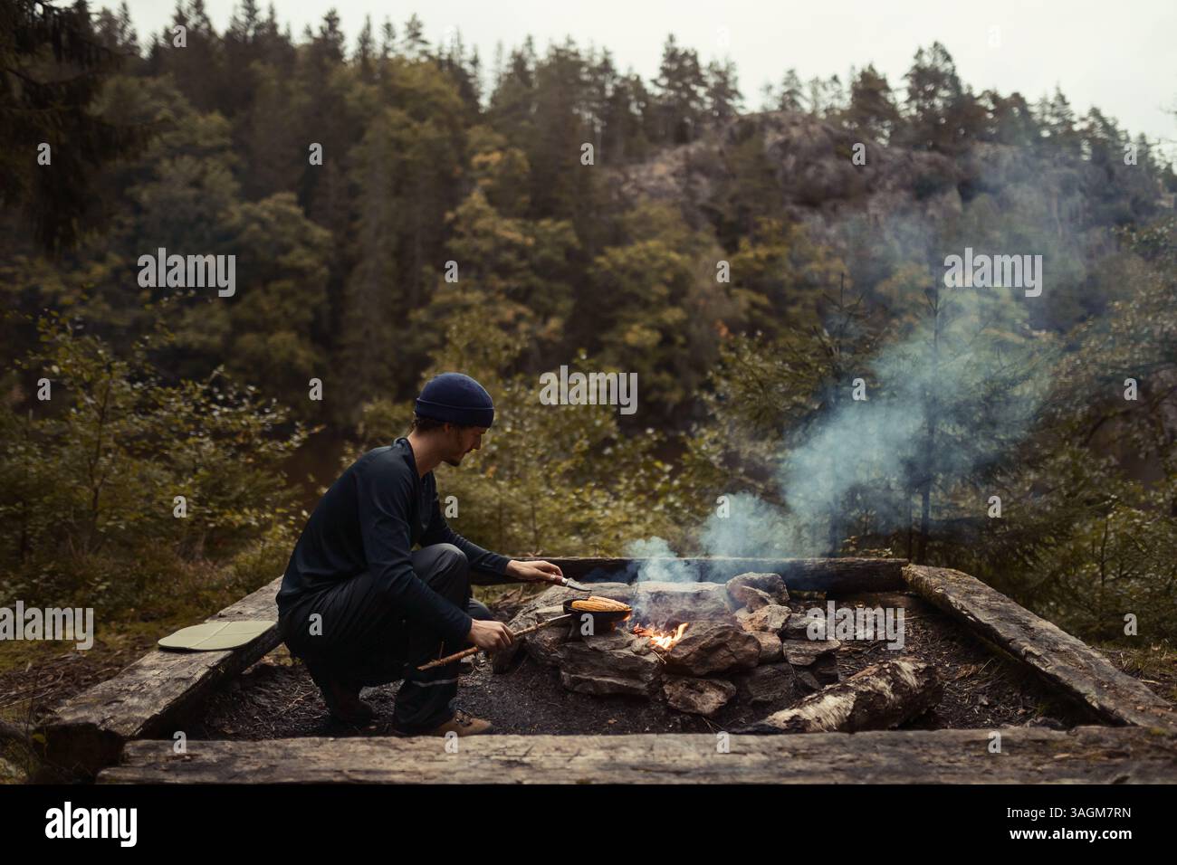 A caucasian man cooking food at a campfire with a frying pan and smoke ...