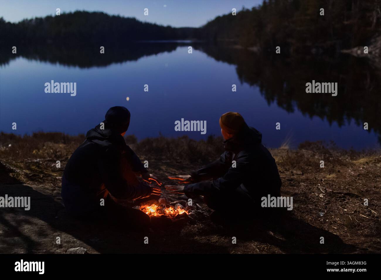 Two caucasian men sitting at a campfire in the forest holding their ...