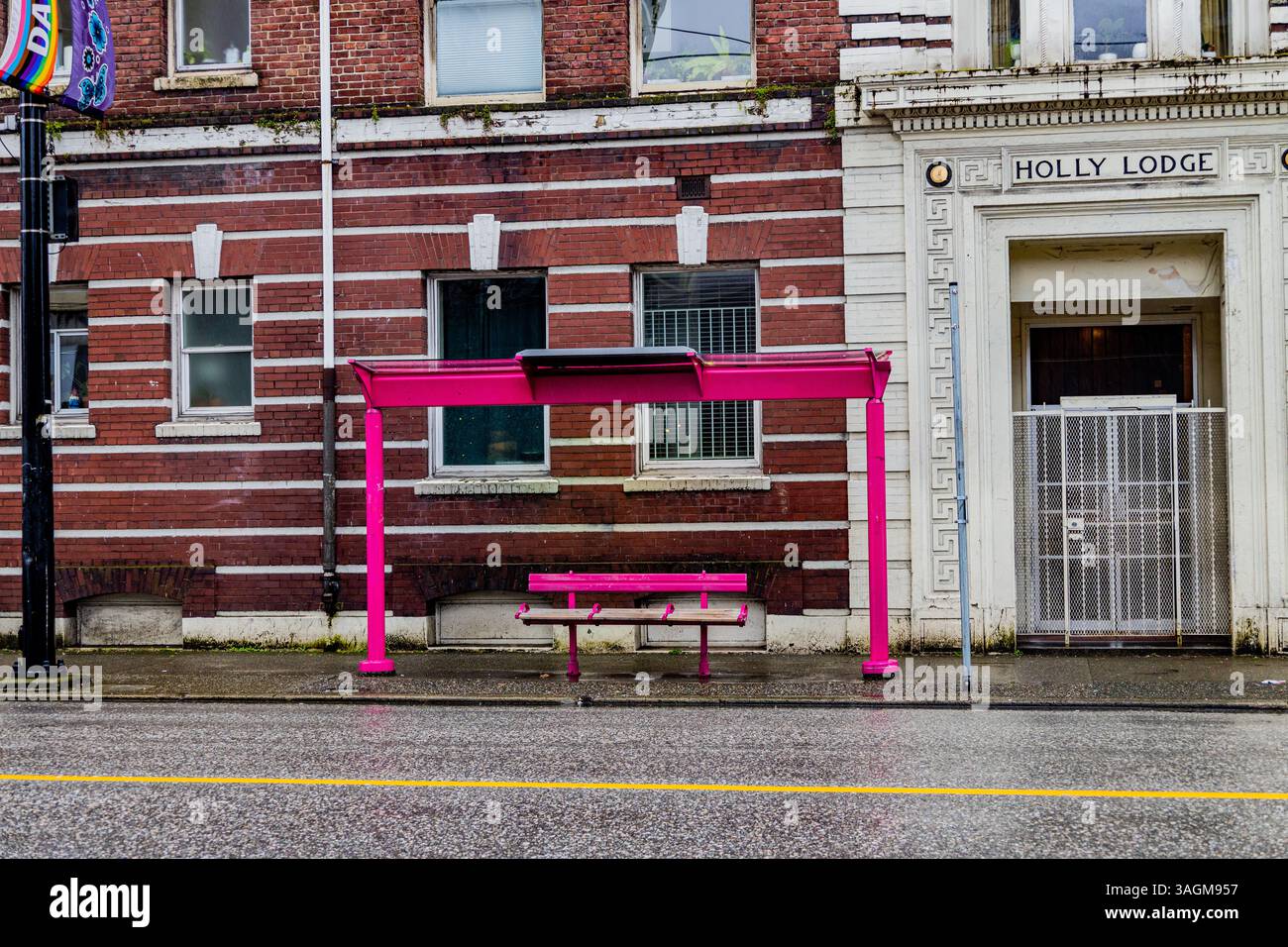 Pink bus stop shelter with a bench in front of a brick building. Wet ...