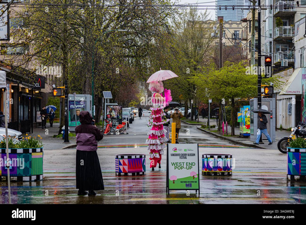A stilt walker in a pink floral costume with an umbrella, festival ...