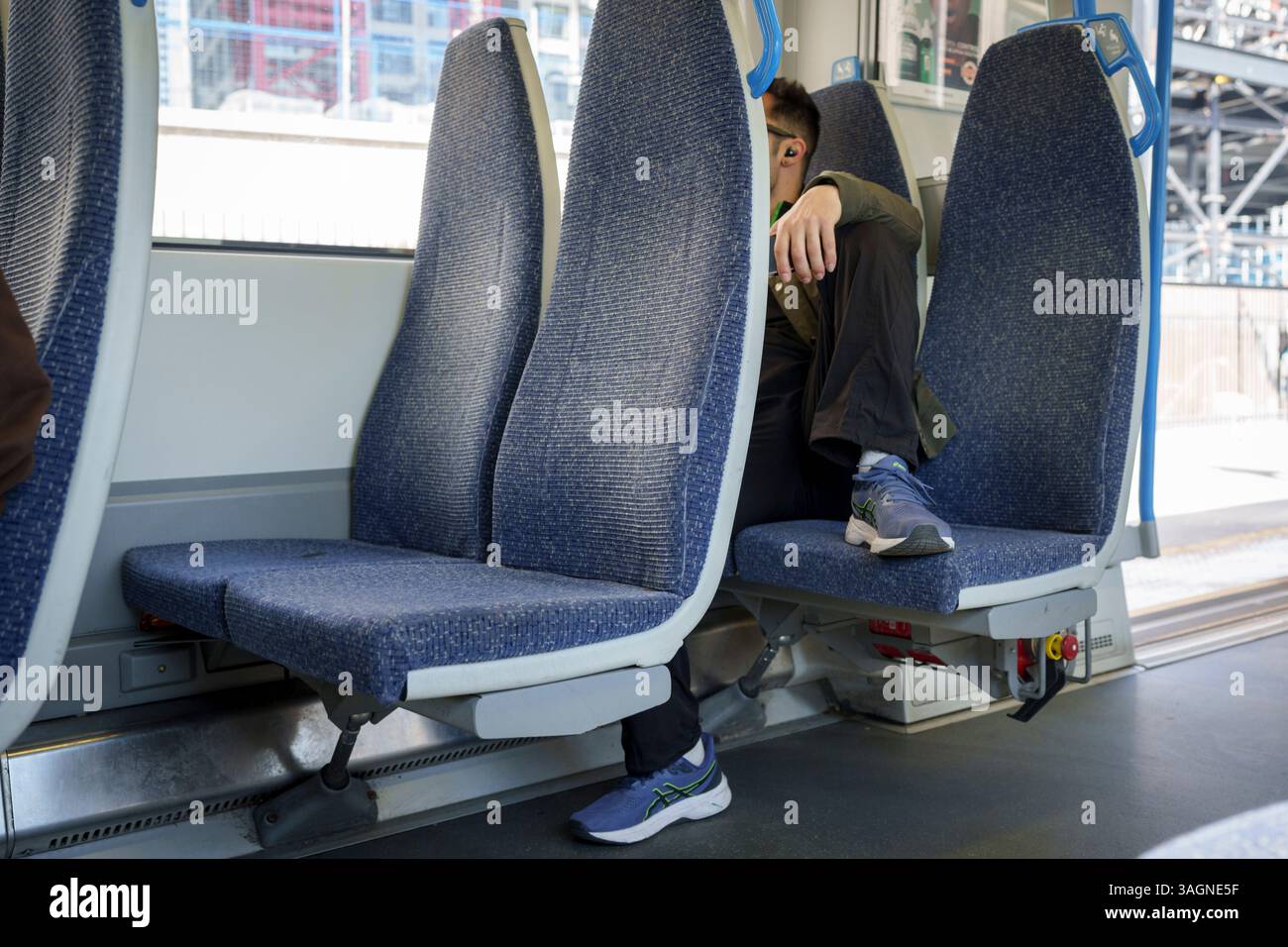 The shoes of a rail passenger rest on the fabric seats of a train ...
