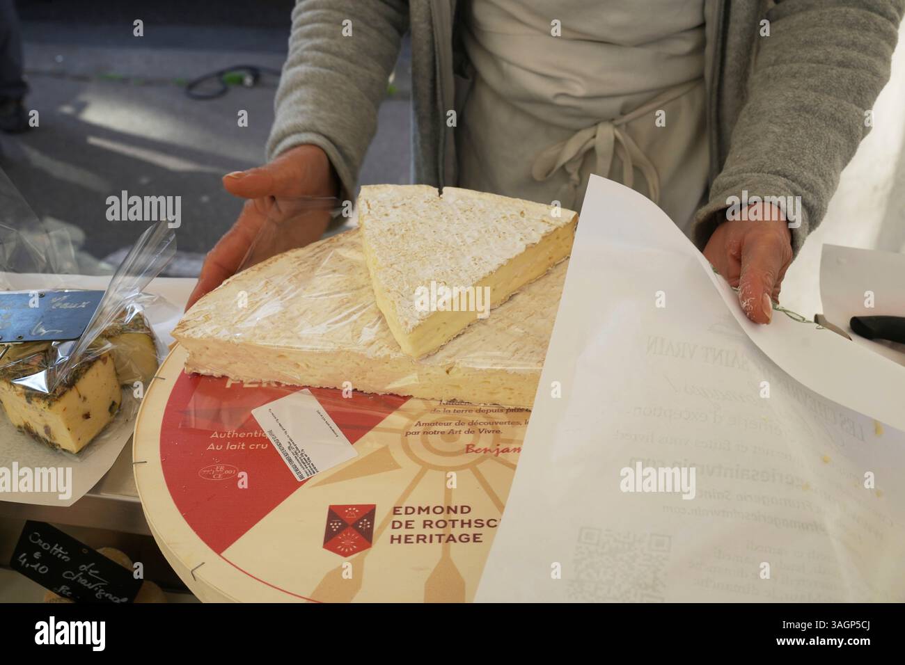 A seller displays a large piece of cheese at an open air market as ...