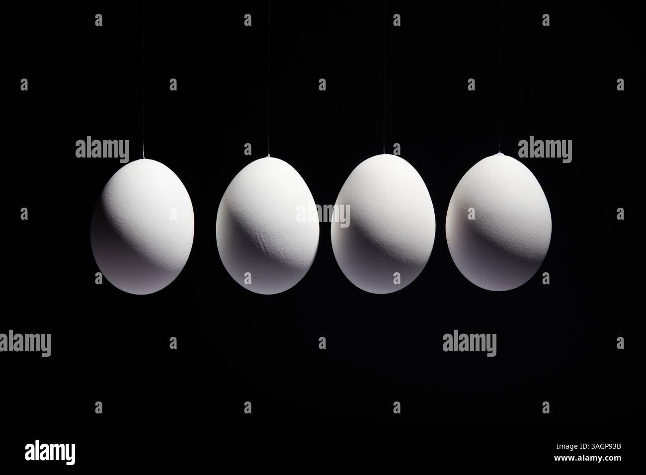 Four white eggs, suspended by thin, unseen strings, are arranged in a ...