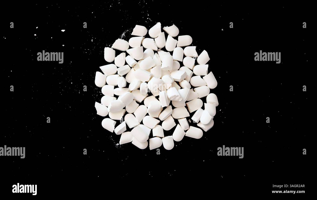 A pile of white supplement tablets, split into half the size. With dark ...
