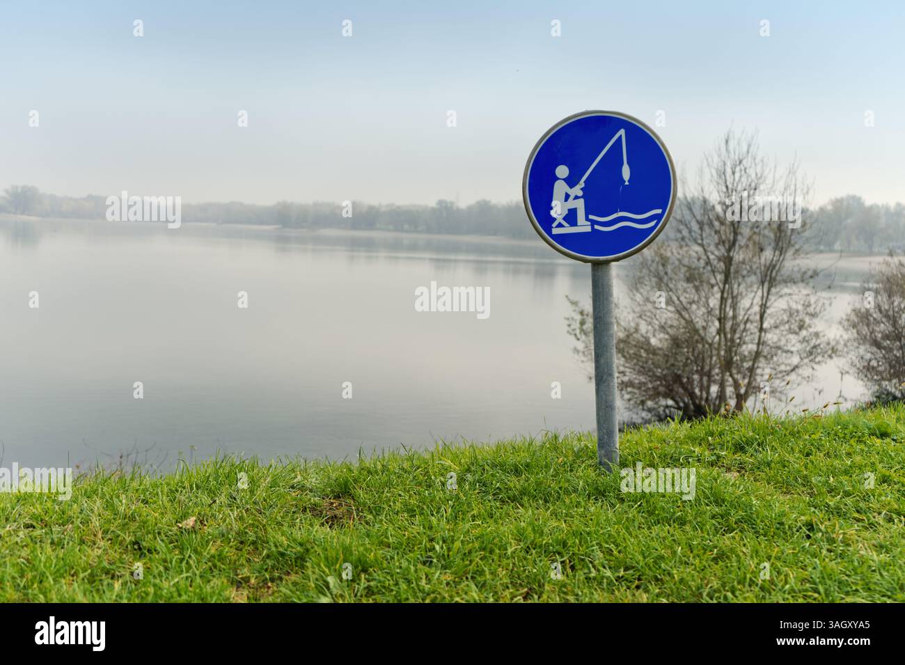 The image shows a sign indicating a designated fishing area by a calm ...