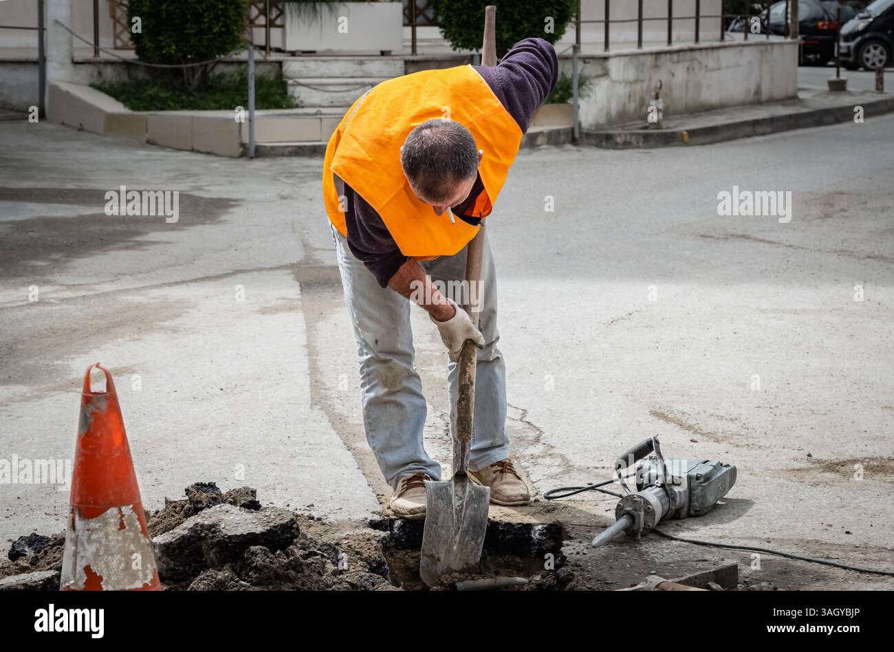 Male construction worker is loading gravel with shovel. Construction workers at work. Worker ...