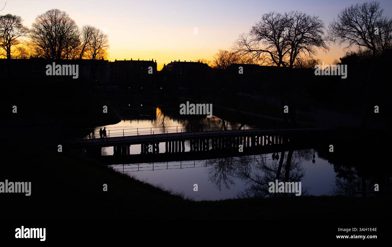 Silhouette of a bridge with reflections in calm water in a park ...