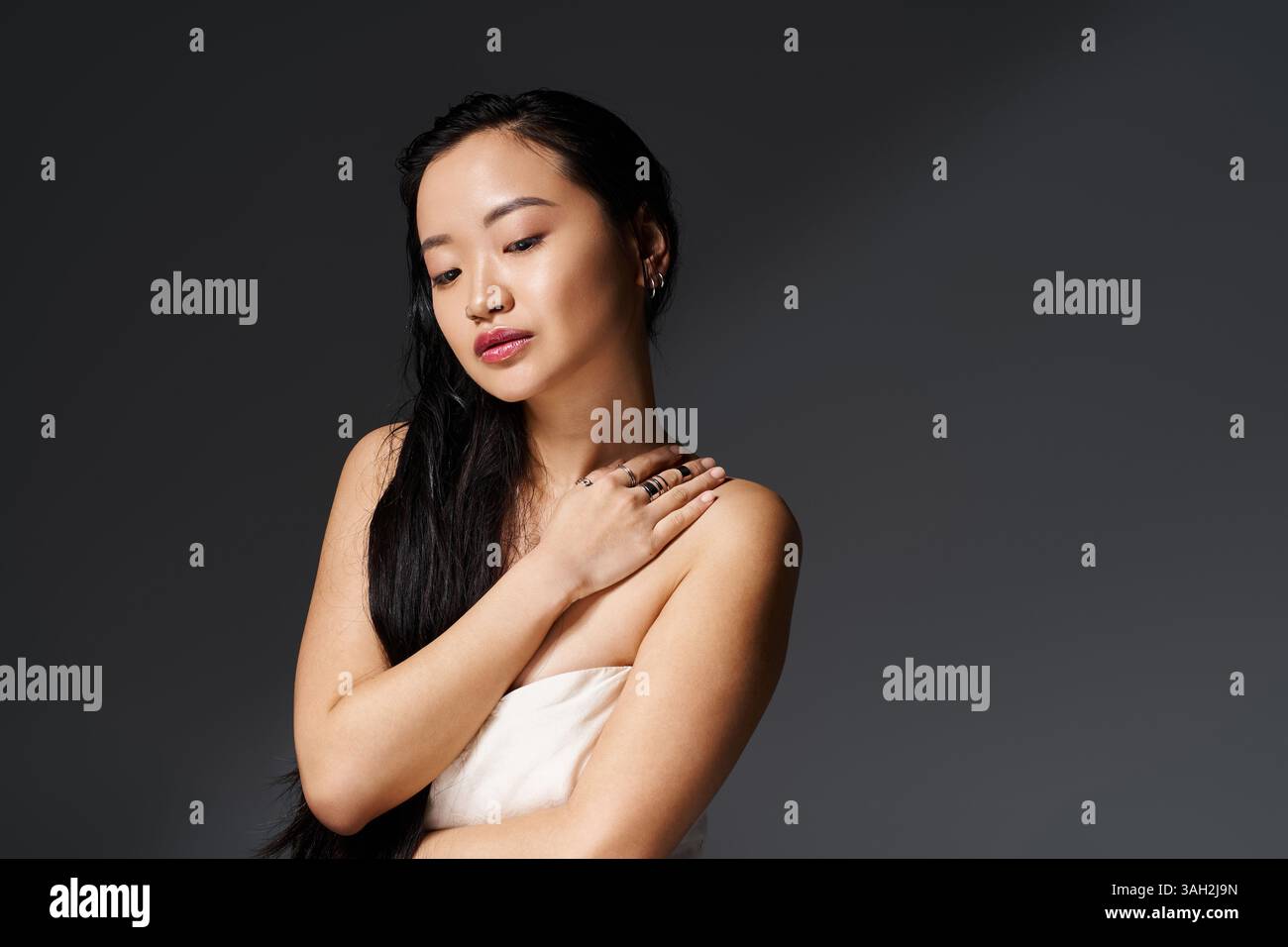 A young Asian woman gracefully poses in a minimalistic studio ...
