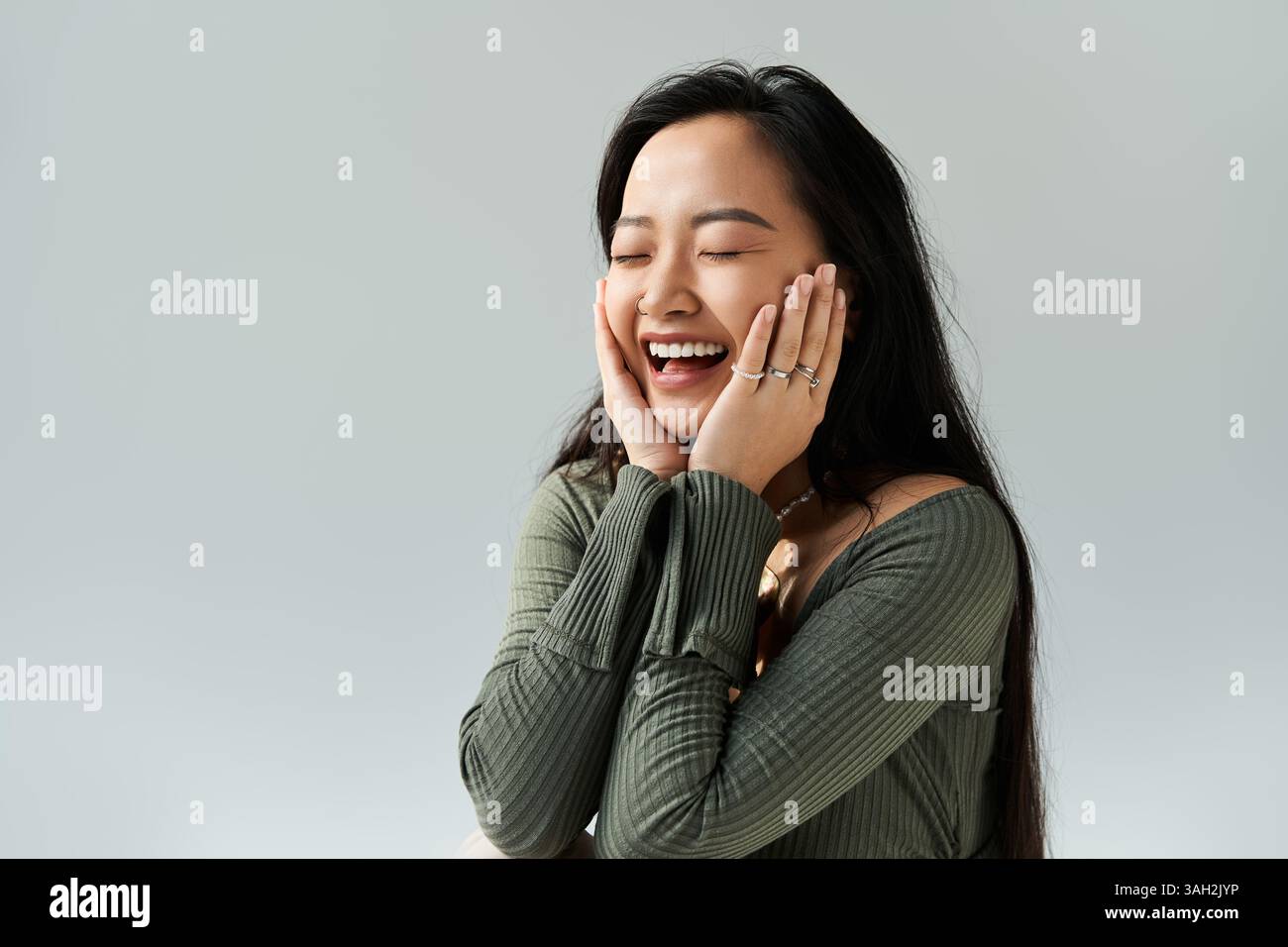 A young Asian woman smiles, her hands on her cheeks, savoring pure joy Stock Photo - Alamy