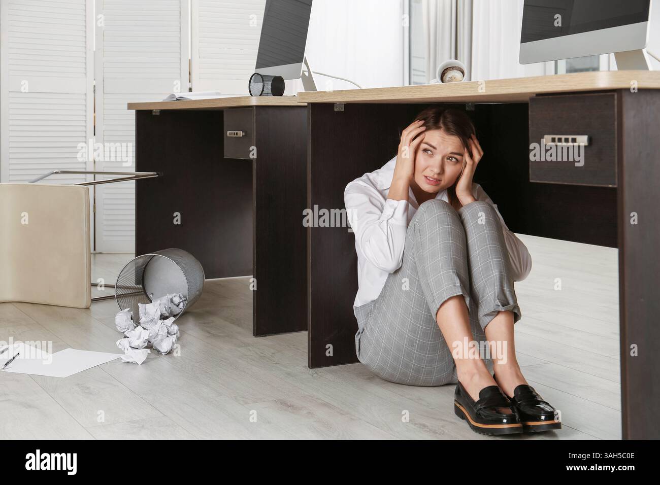 Scared young woman hiding under office desk during earthquake Stock ...