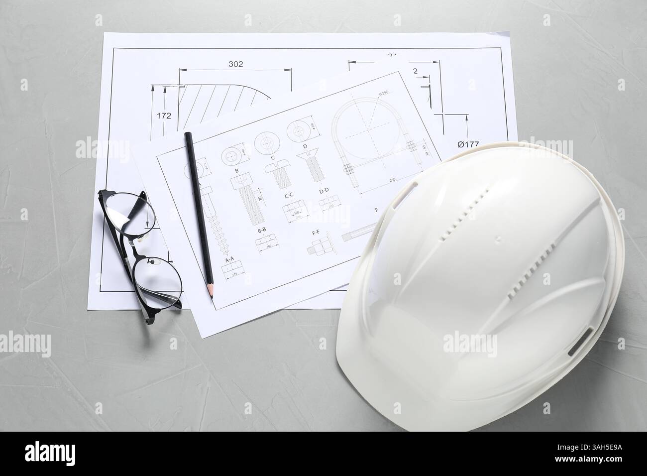 Different engineering drawings, hard hat, pencil and glasses on grey ...