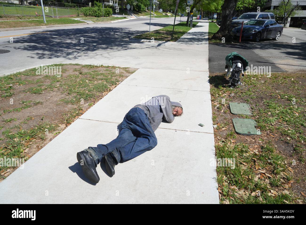 A homeless man takes a morning nap on the public sidewalk outside a ...