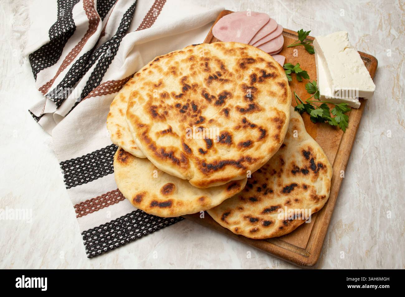 Fried pita bread stack on a wooden chopping board with ham slices and ...