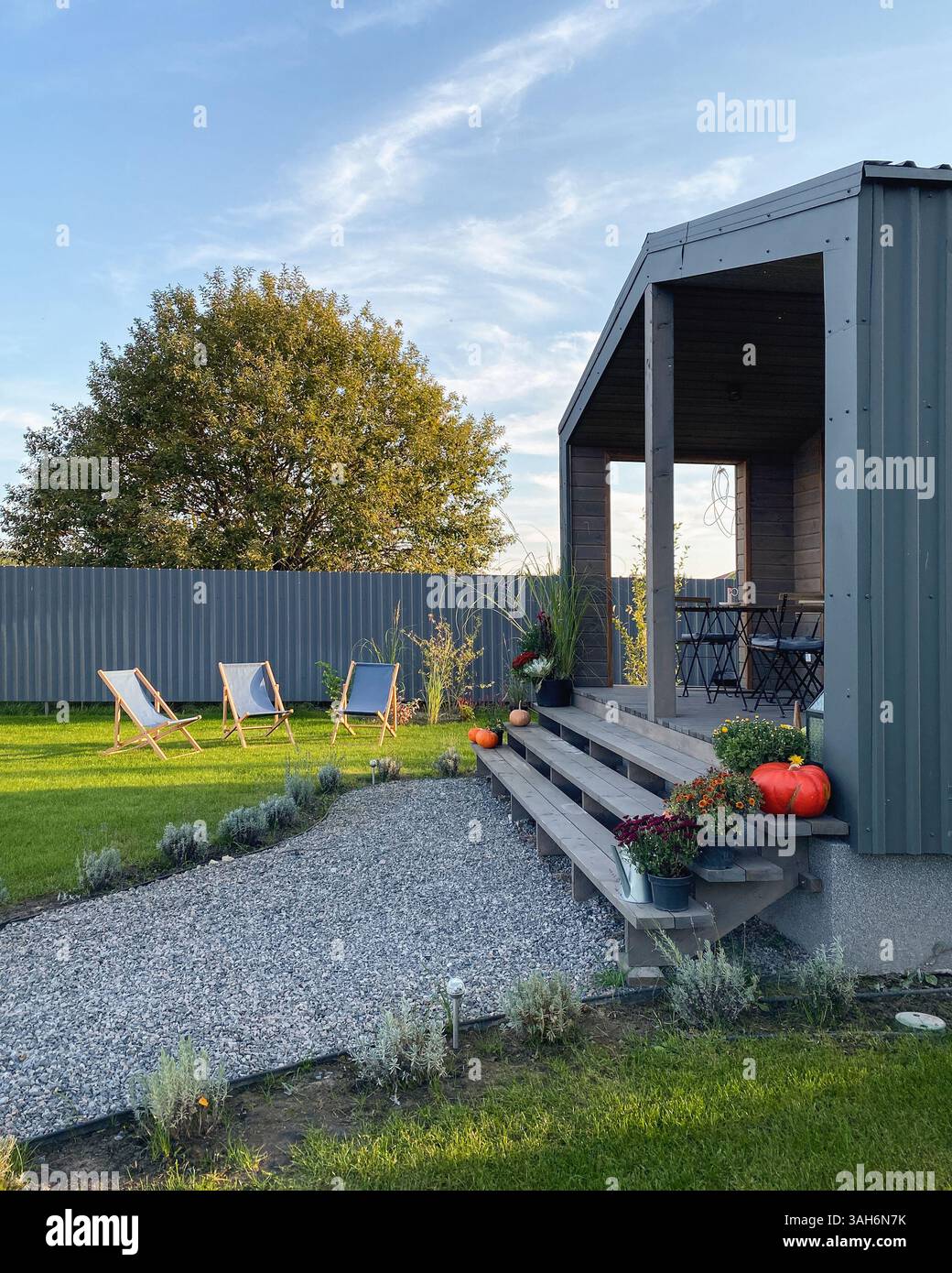 Modern summer house in rays of morning sun, lawn and fenced yard around ...