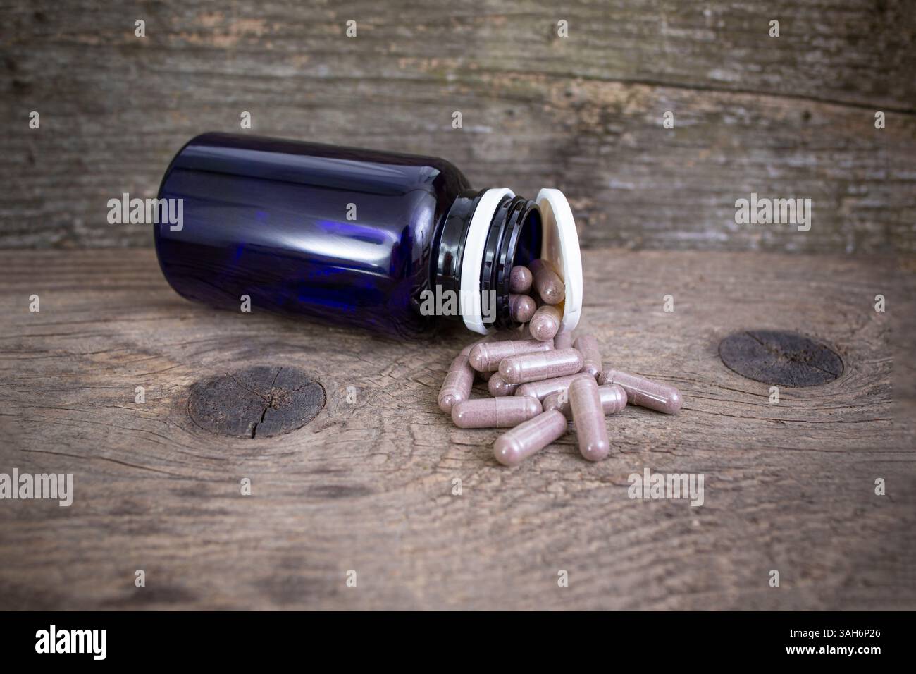Blue pill container spilling grey capsules on weathered wood background ...