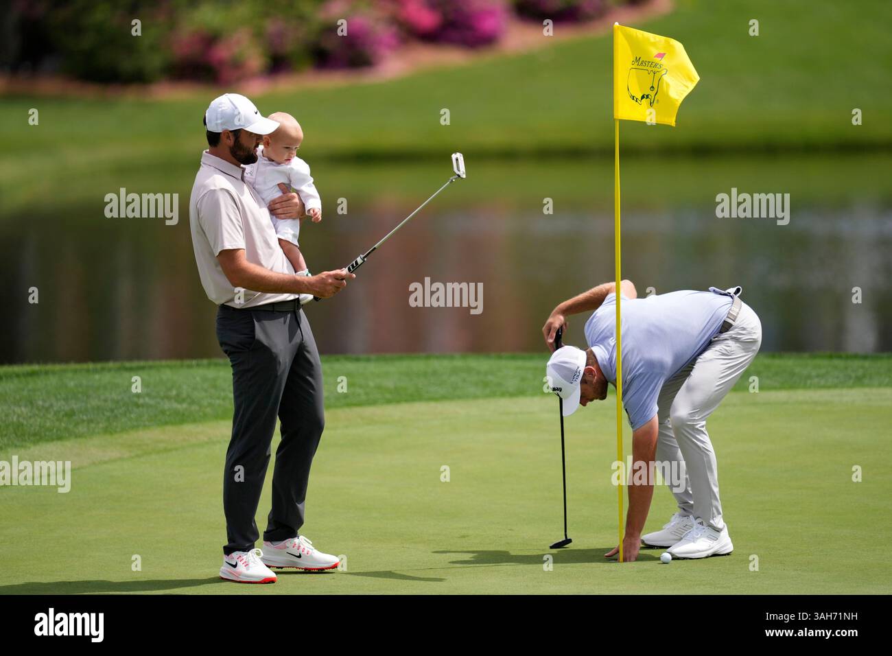 Scottie Scheffler holds his child Bennett as Sam Burns removes his ball ...