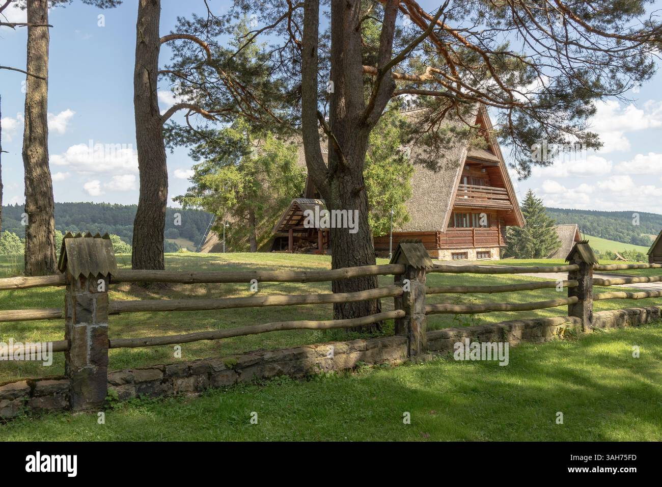 A house with a slanted roof sits in a field with a fence around it. The ...