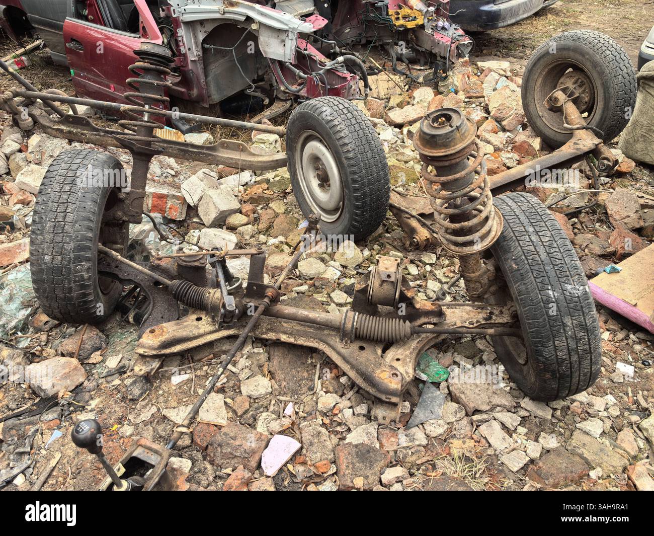 Old car frames and wheels lie among piles of rubble in a junkyard. Rust ...