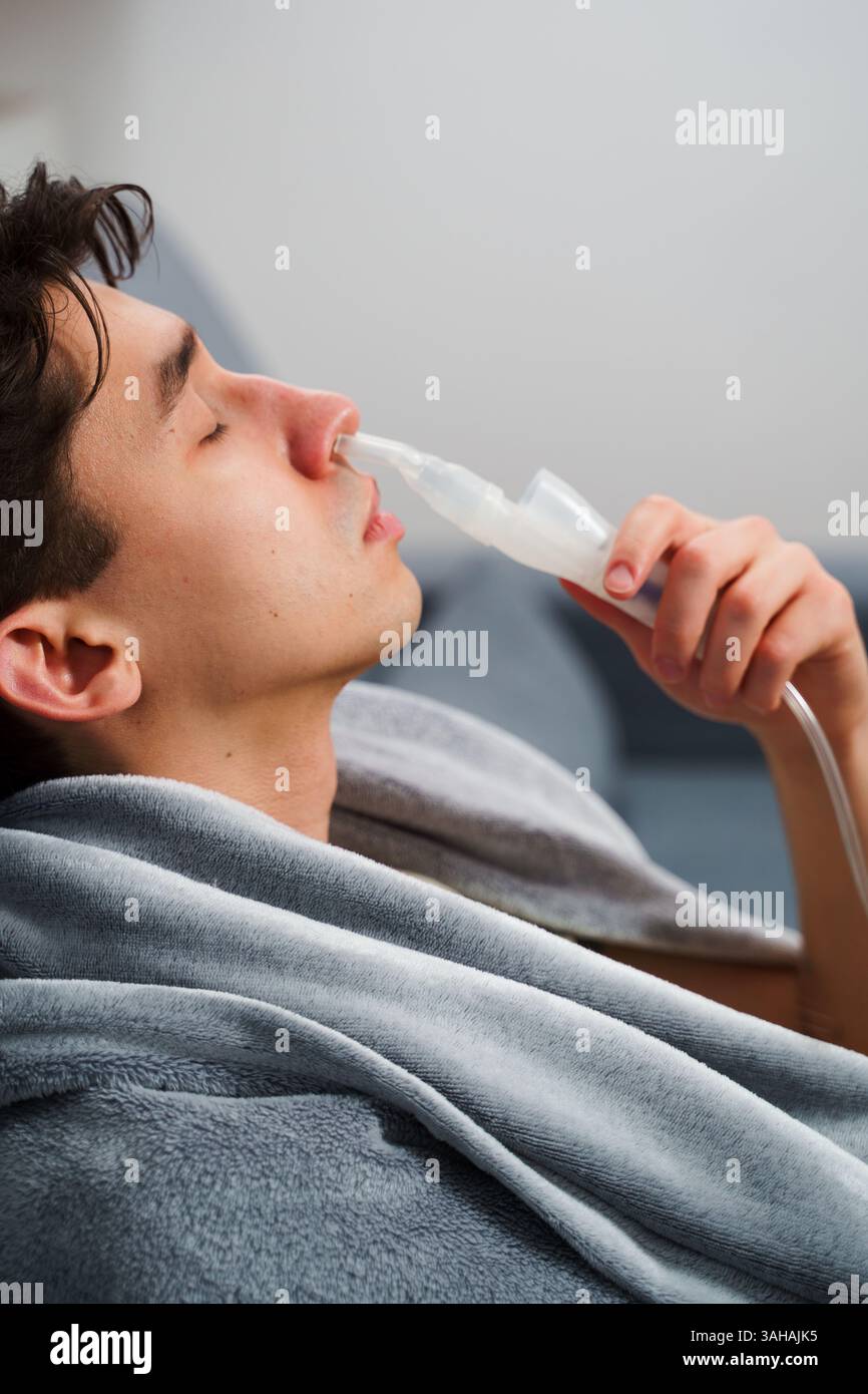 Young man with asthma attack breathing with inhaler in the bad. Doing ...
