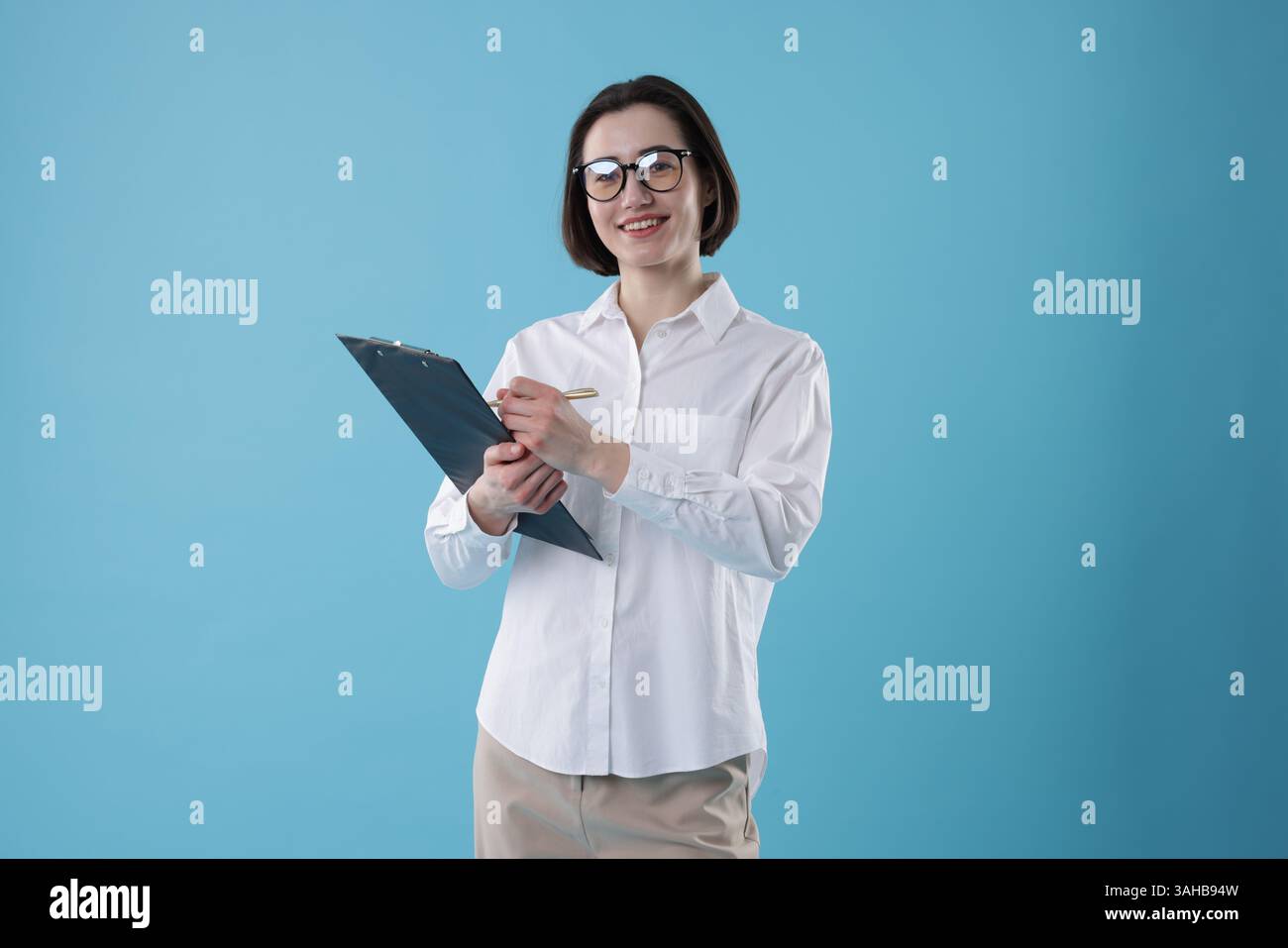 Young secretary with clipboard taking notes on light blue background ...