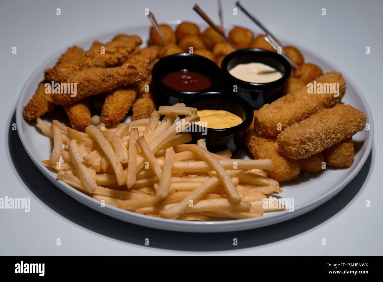 Assortment of fried fast food on a white plate with dips, including ...