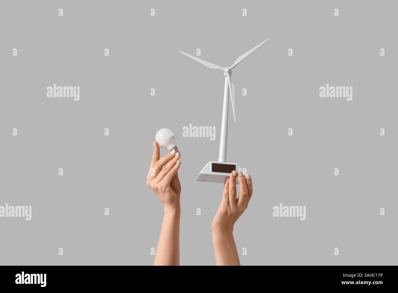 Female hands with wind turbine model and light bulb on light background ...