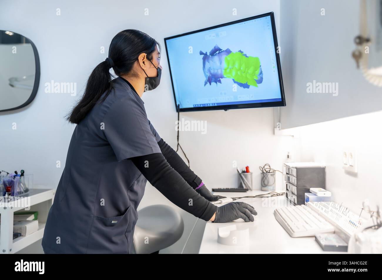 Dentist wearing a face mask and gloves using a computer and analyzing a ...