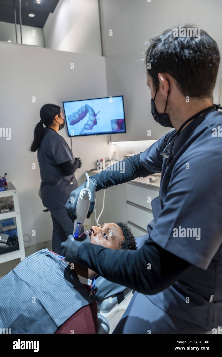 Dentist using intraoral scanner on patient's teeth, with dental ...