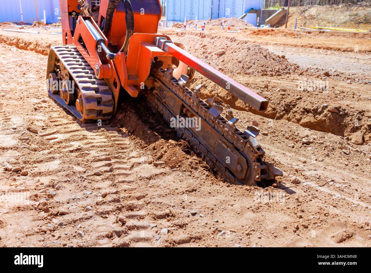 Excavator operates on construction site, digging trench in soil while ...