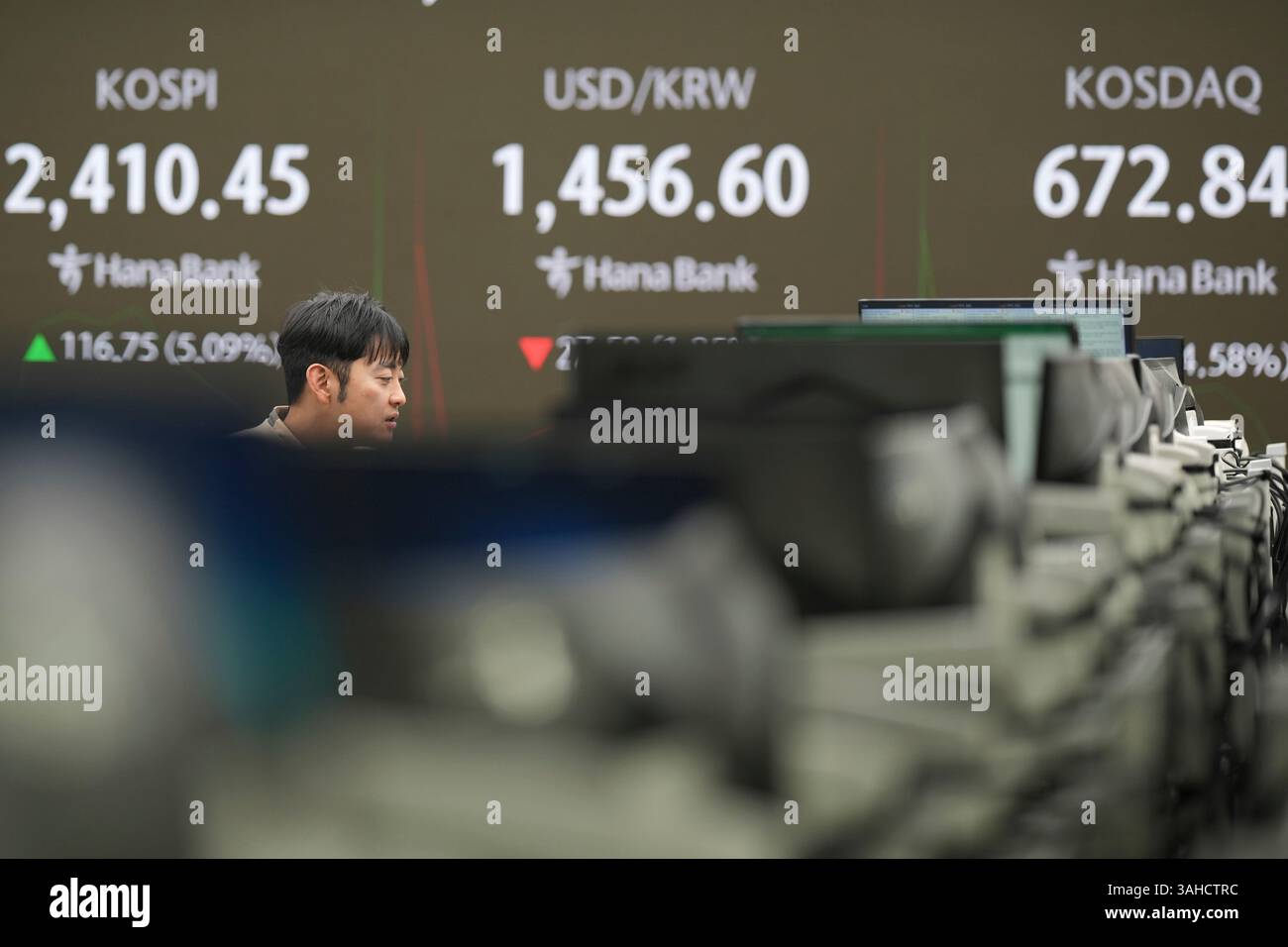 A currency trader walks by the screens showing the Korea Composite Stock Price Index (KOSPI ...