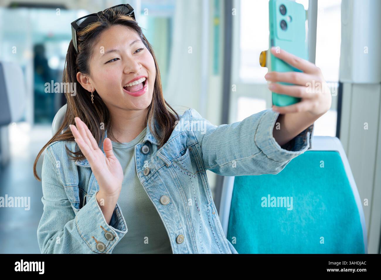 Smiling chinese woman taking selfie on public transport while flashing peace sign joyfully Stock ...