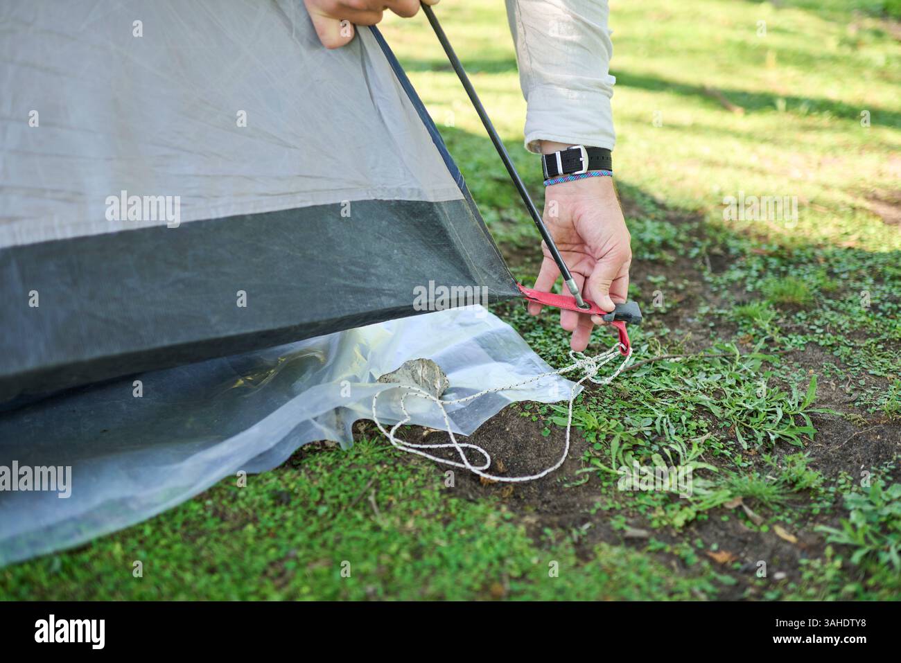 Unrecognizable man putting up the poles of his tent, in the process of ...