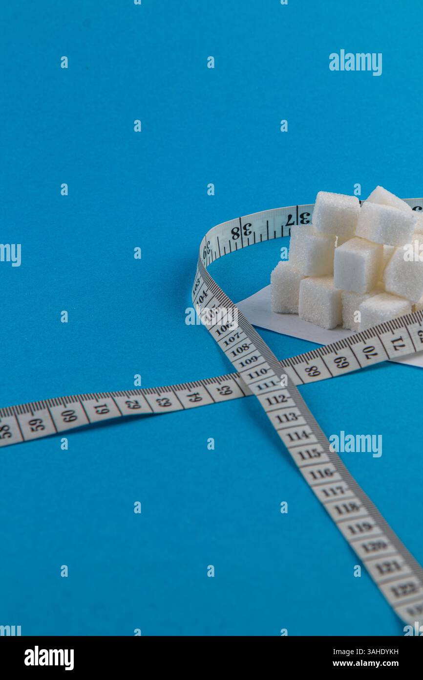 Sugar cubes are stacked on a flat surface next to a measuring tape ...