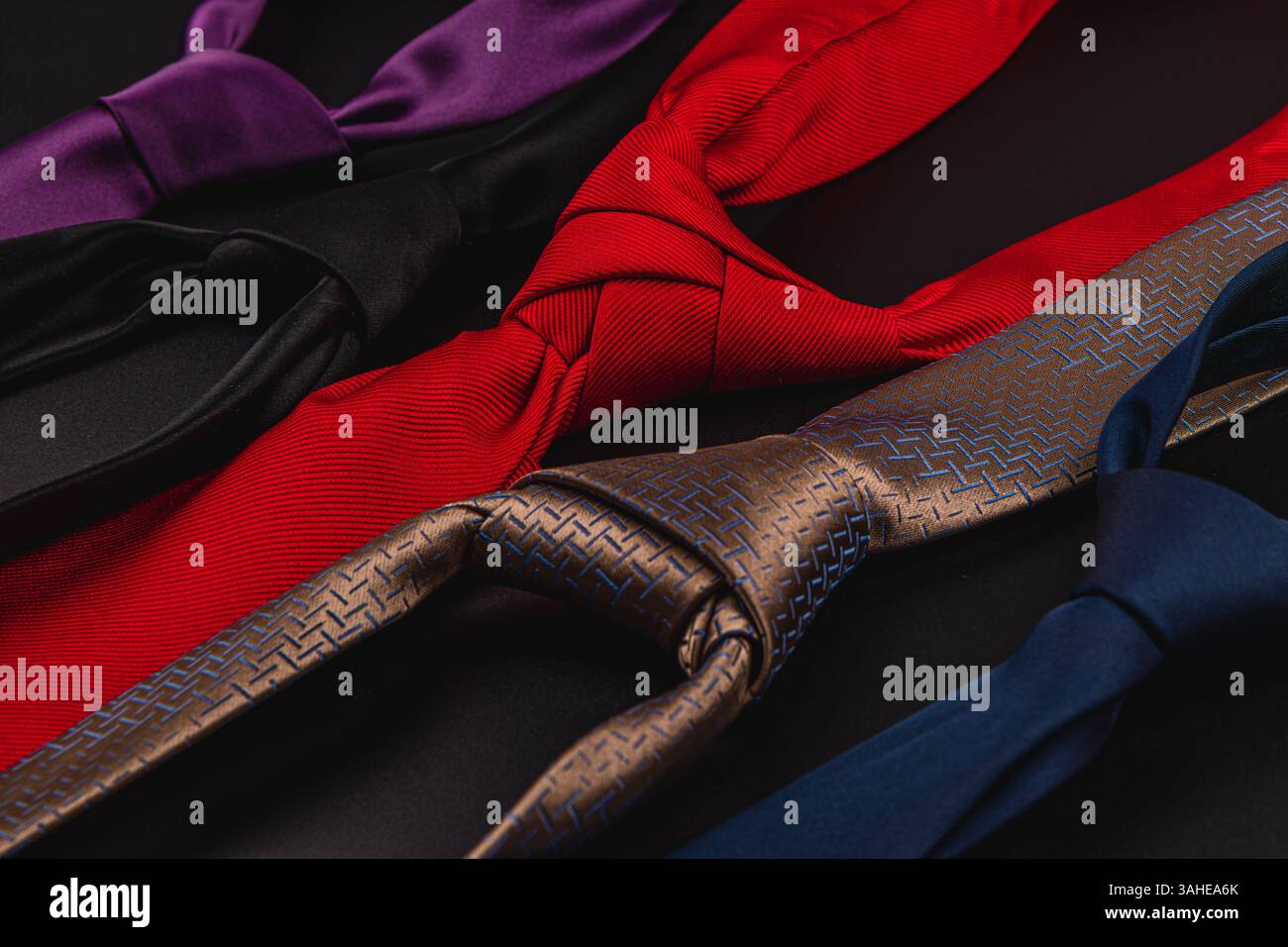 Different stylish ties in vibrant colors are arranged on a dark surface ...