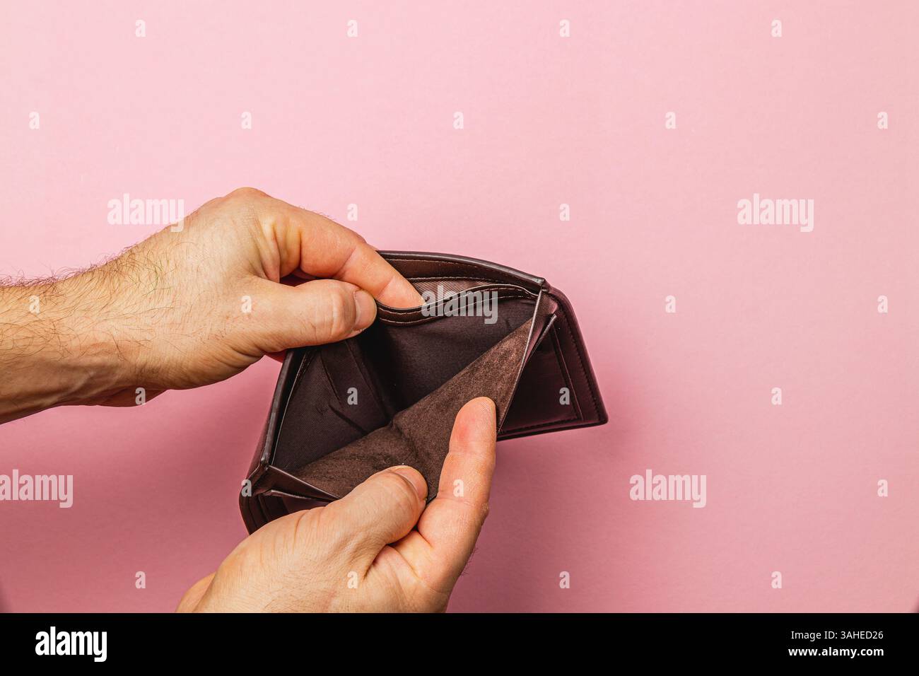 A male businessman examines his empty leather wallet with concern ...