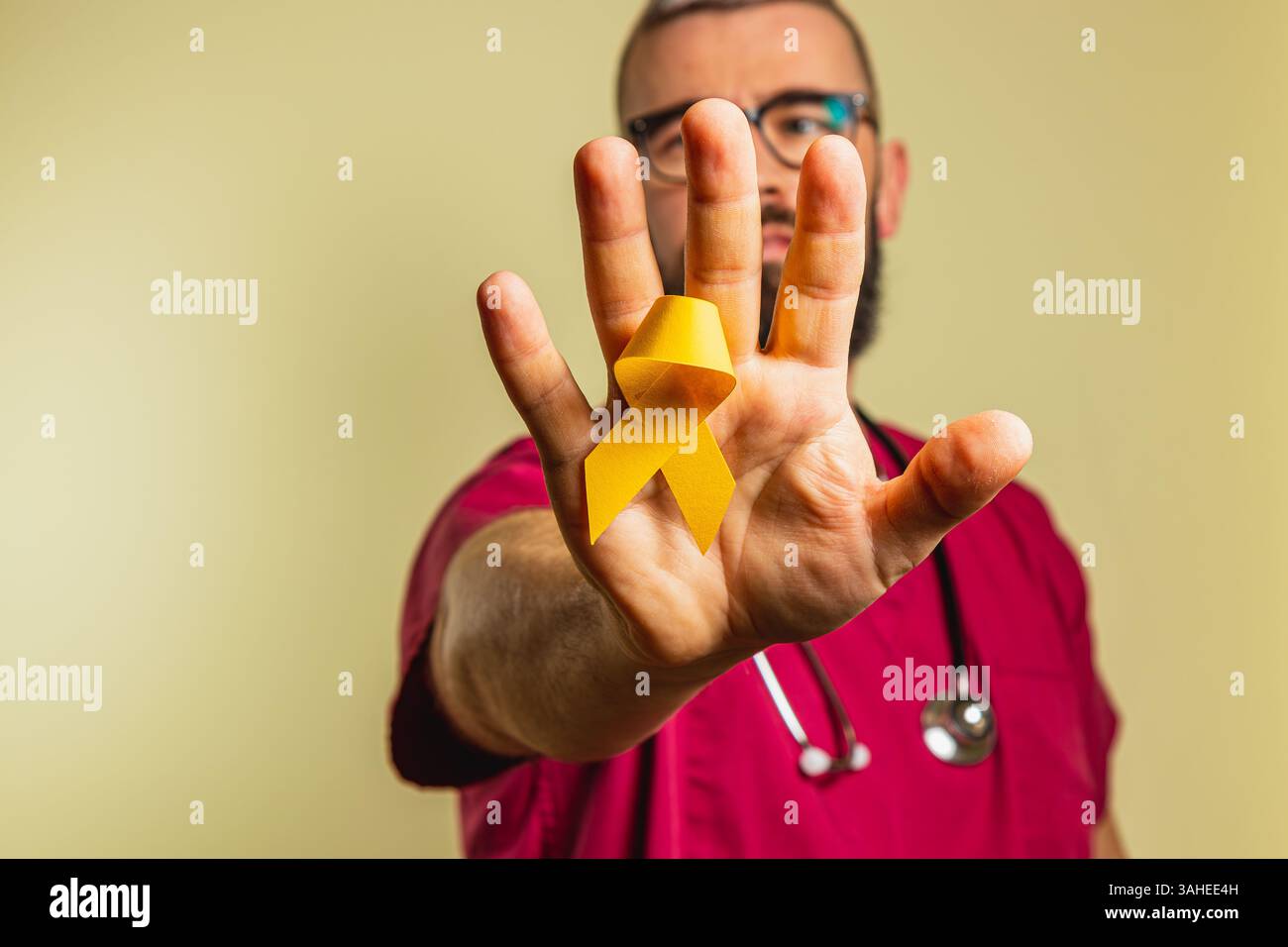 A young male medic wearing scrubs holds up a yellow ribbon against a ...