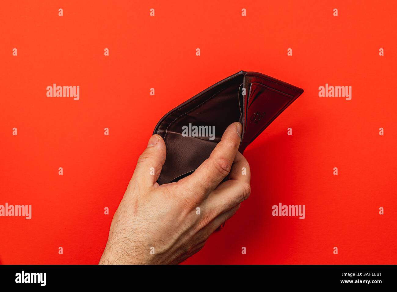 A man holds an empty leather wallet against a bright red background ...