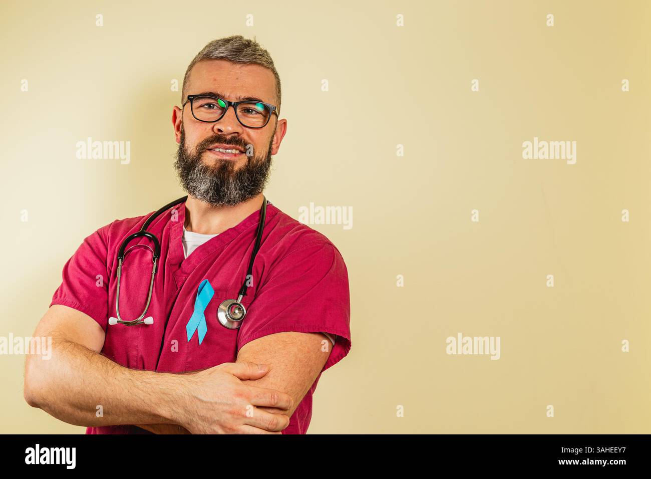 A young male doctor wearing maroon scrubs and glasses stands ...