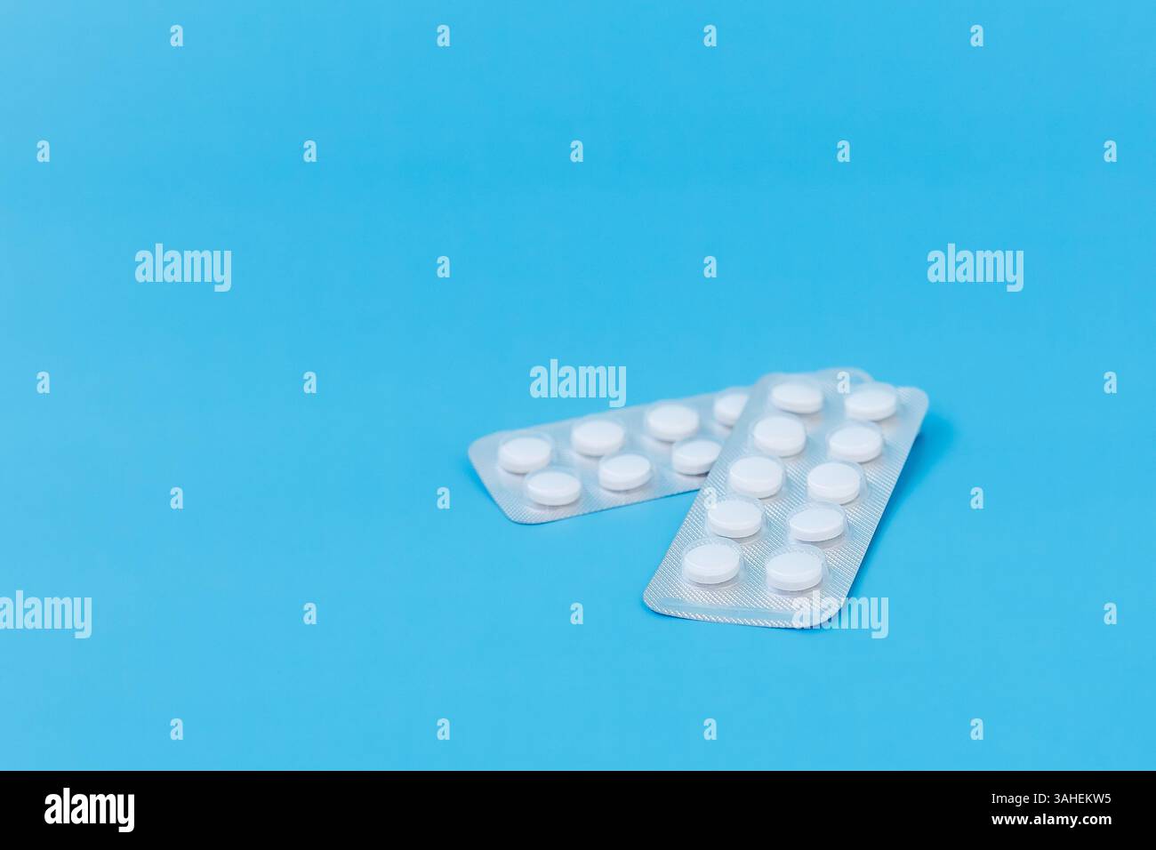 Two blister packs of white round tablets placed on a clean blue ...