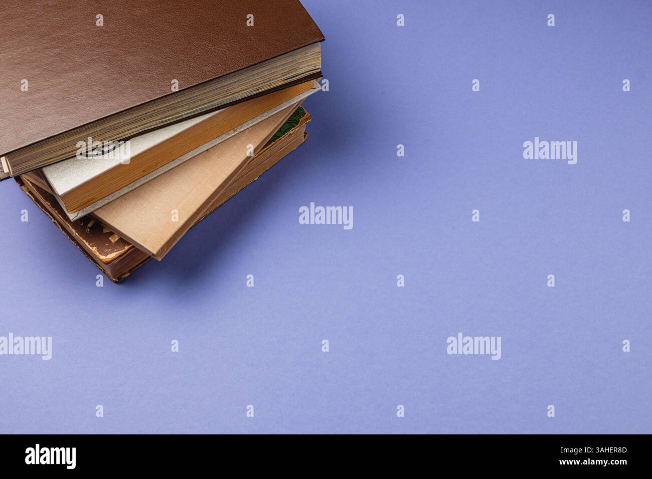 A collection of vintage books is stacked on a smooth light purple ...