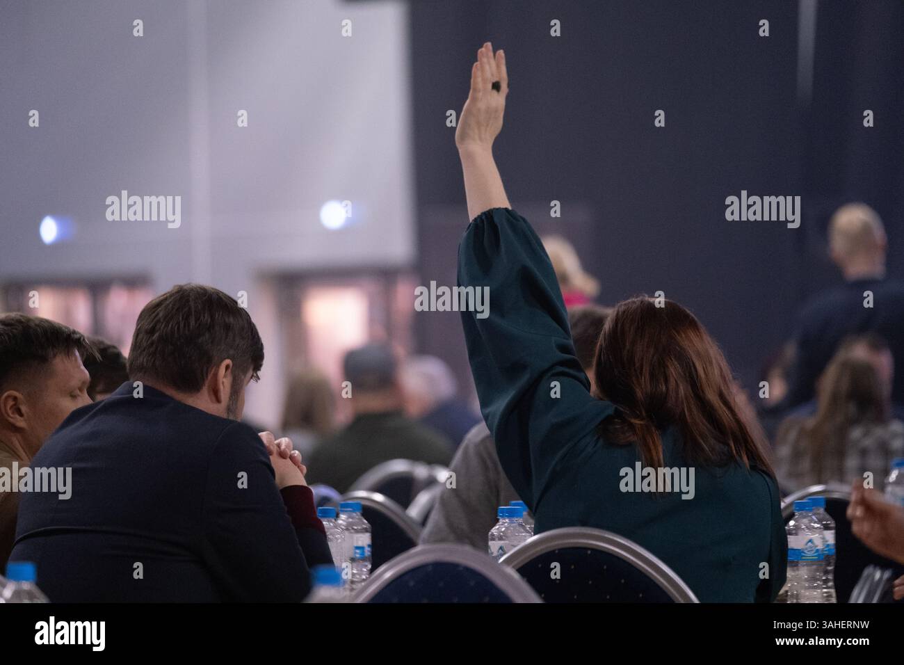Audience member raises hand in conference setting while seated among ...
