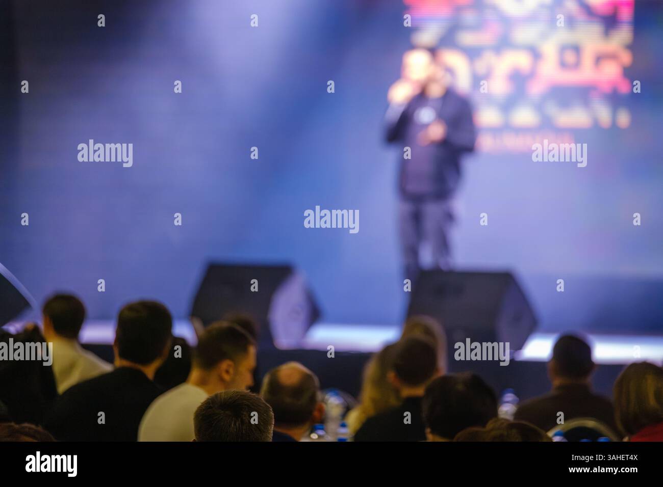 Blurry speaker on stage with an audience seated and focused on the event Stock Photo - Alamy