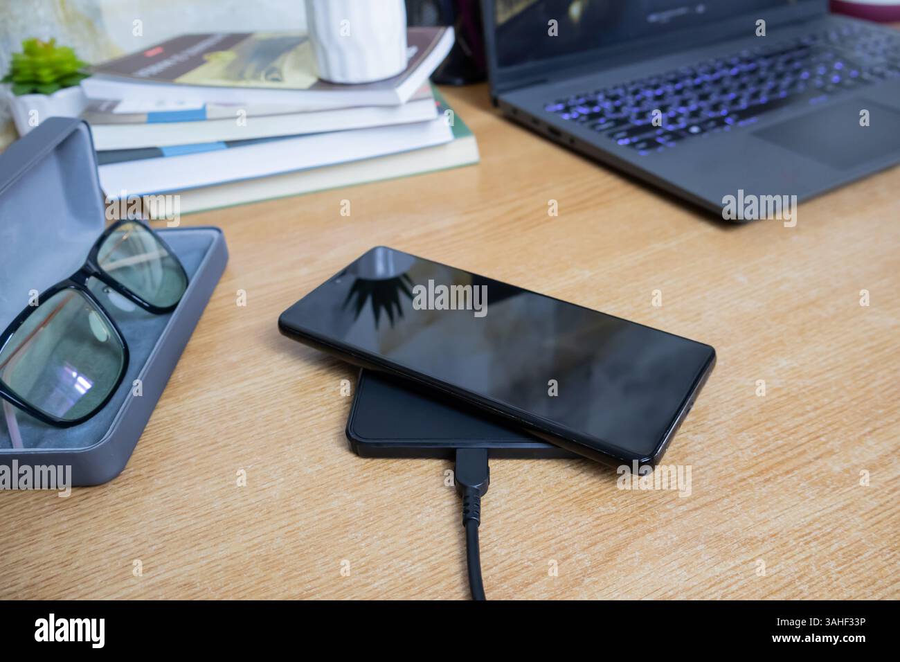 Smartphone placed on wireless charging pad on working table, top view ...